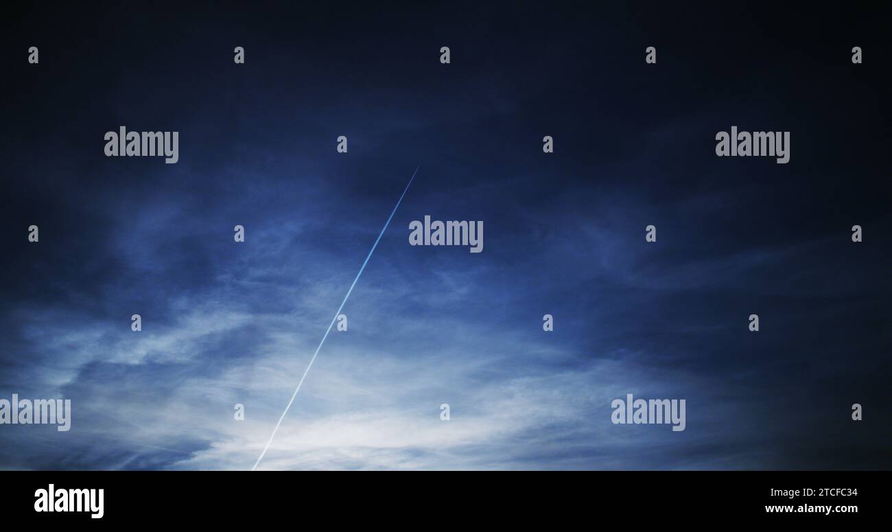High altitude aircraft with bright, glowing contrail in the deep-blue ...