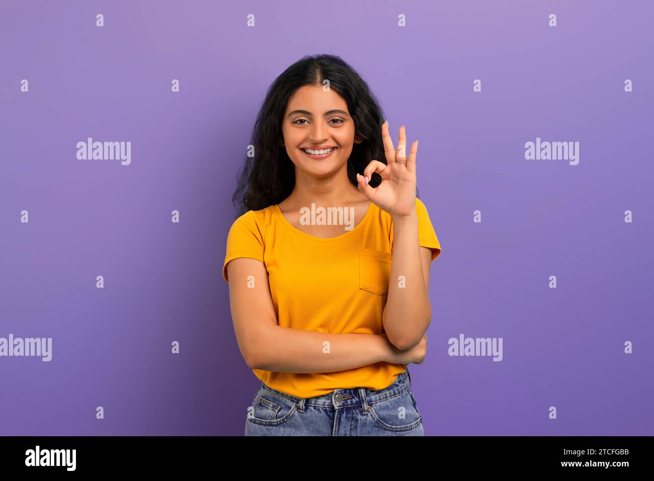 Positive young indian woman showing okay gesture on purple background ...