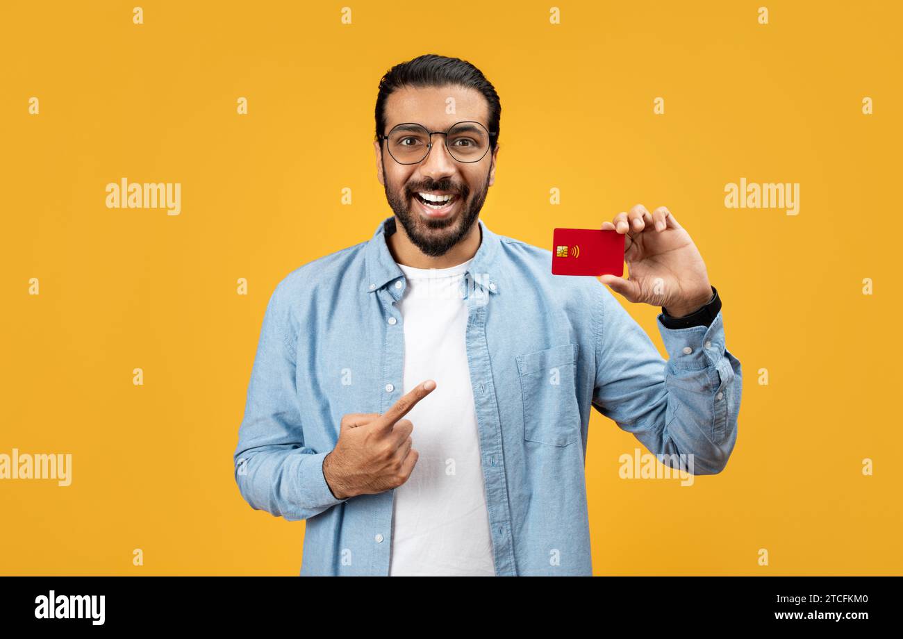 Happy man in a blue shirt proudly pointing at a red credit card in his ...