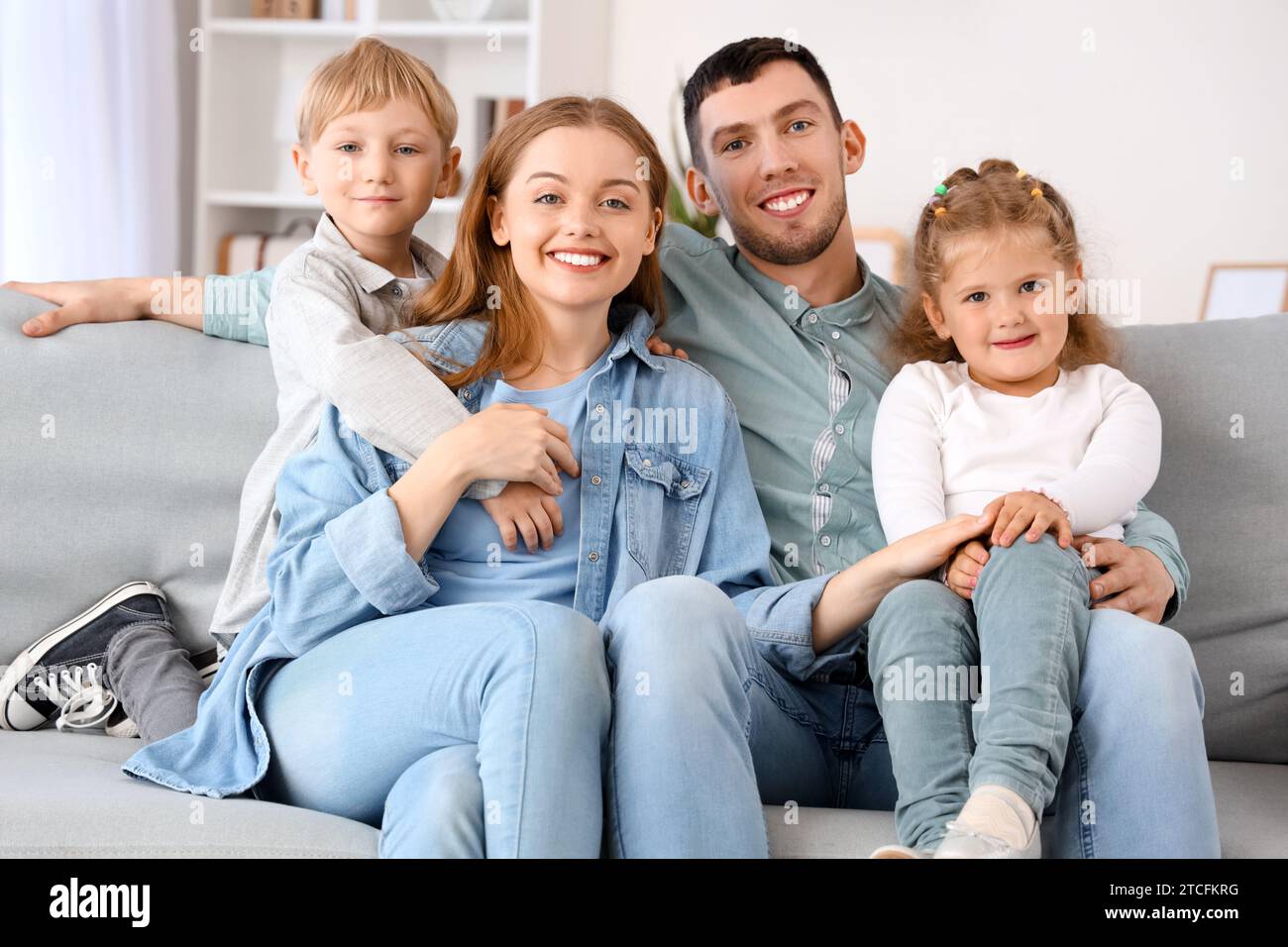 Happy little children with their parents hugging on sofa at home Stock ...