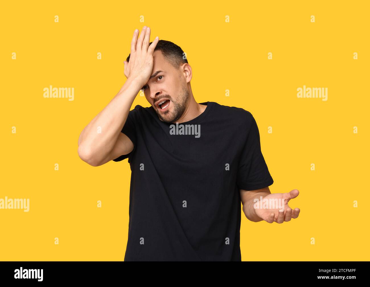 Handsome ashamed young man covering face with hand on yellow background ...