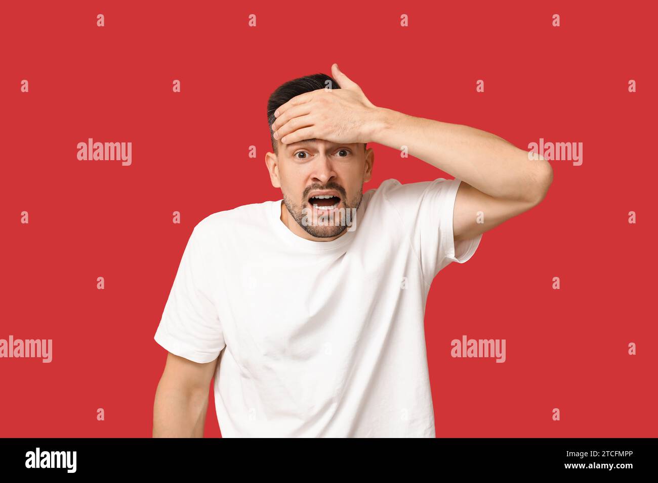 Handsome ashamed young man covering face with hand on red background ...