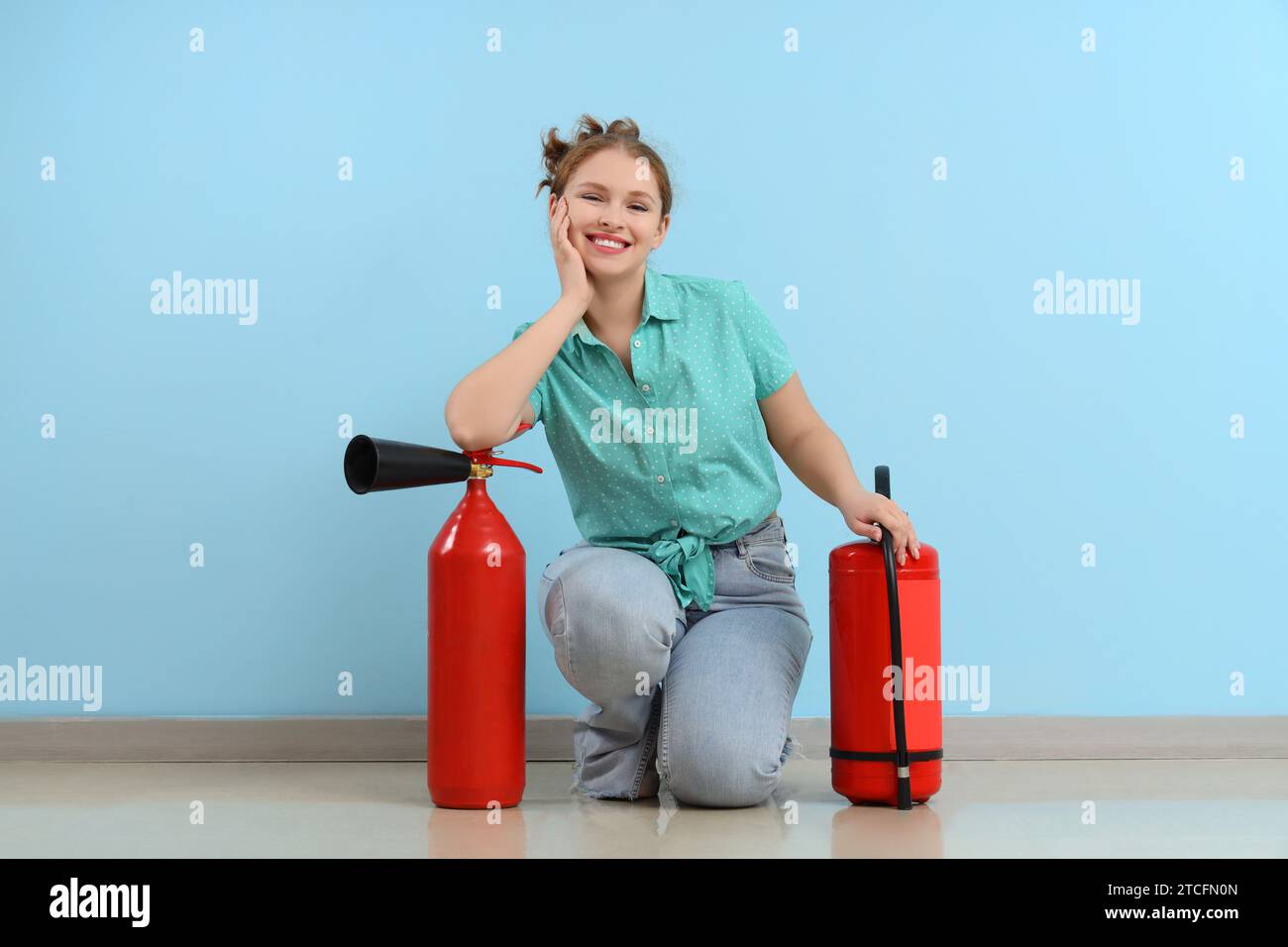 Young woman with fire extinguishers near blue wall Stock Photo - Alamy