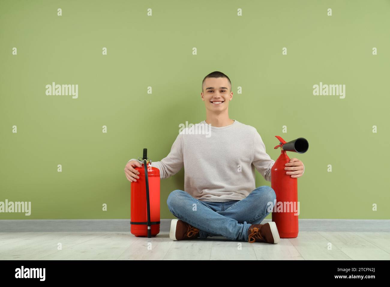 Teenage boy with fire extinguishers sitting near green wall Stock Photo ...