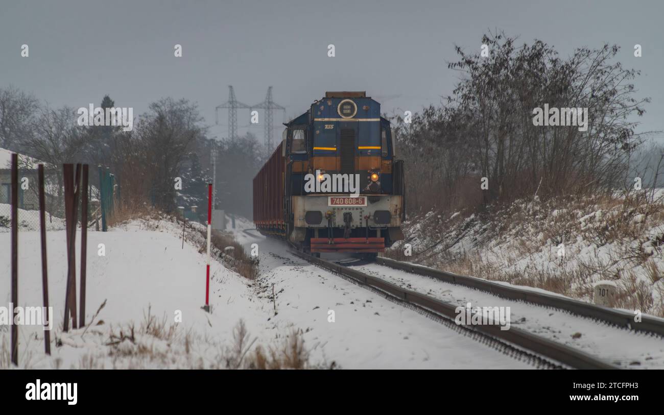 Cargo train with motor engine in winter snowy morning near cold village ...