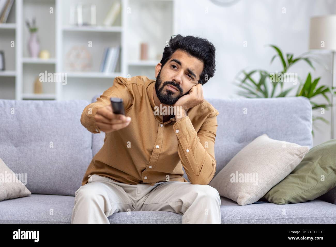 A young Indian man sits and rests tiredly at home on the sofa, uses the ...