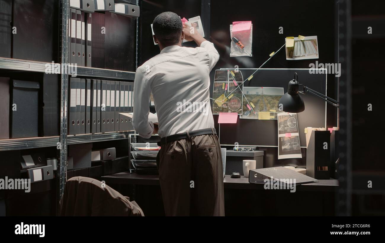 Detective sitting at desk analyzing evidence map on wall, examining law ...