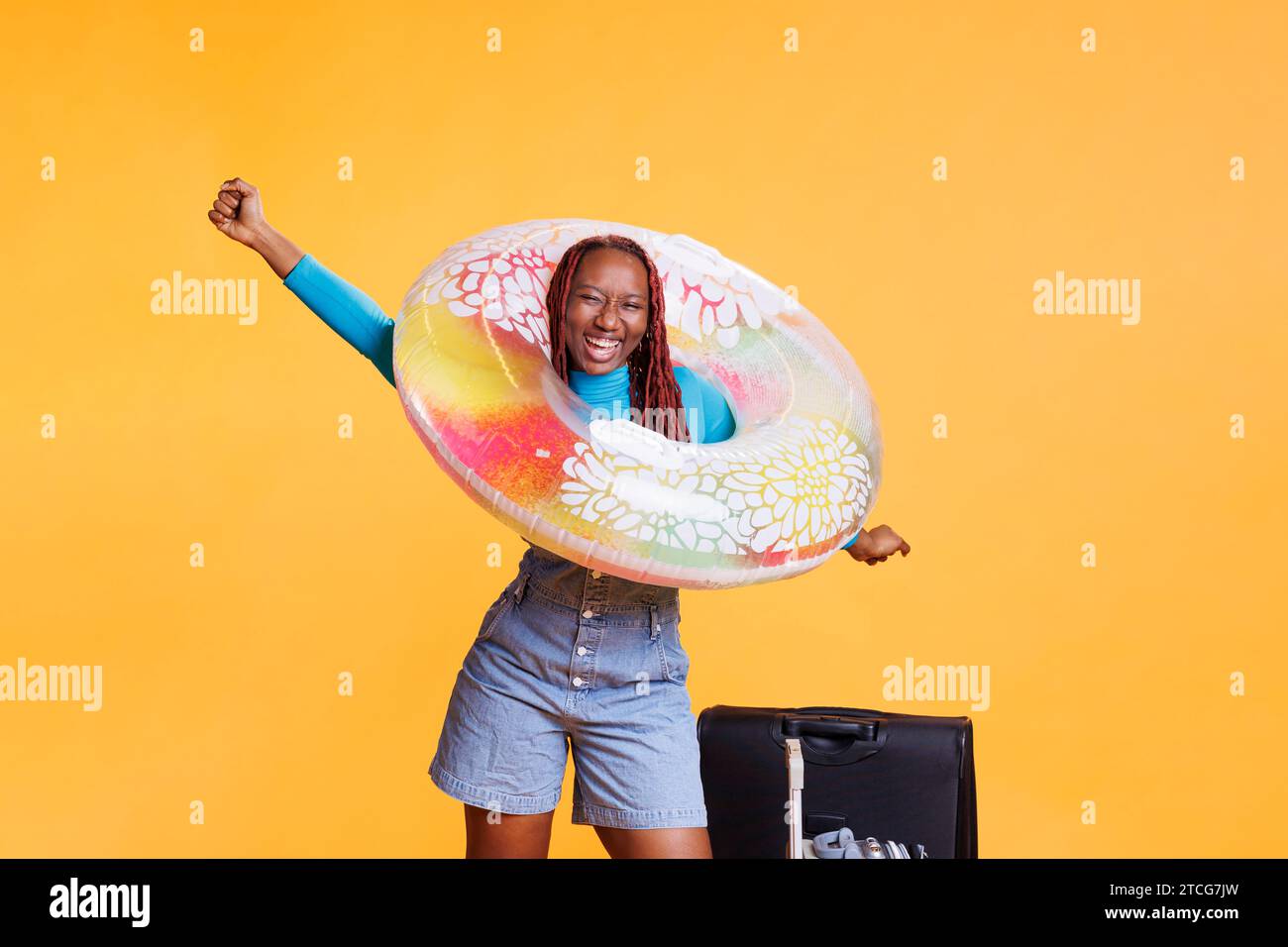 Excited young woman posing in studio with inflatable and suitcase ...