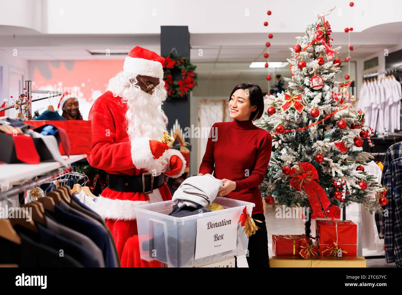 Asian woman helping with charity donations in clothing store, working with santa claus man to ...