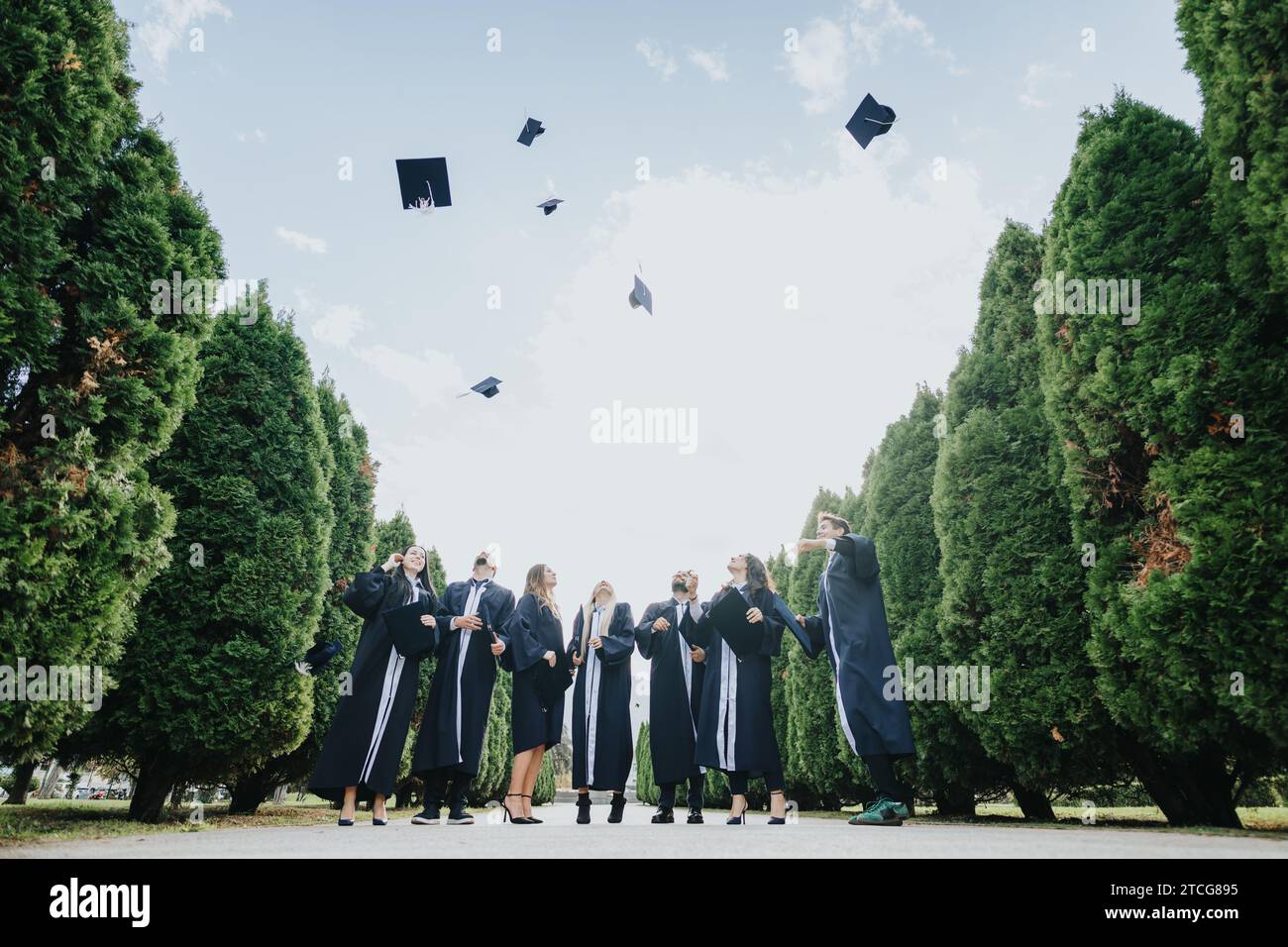 Happy students in graduation gowns, throwing caps as they celebrate ...