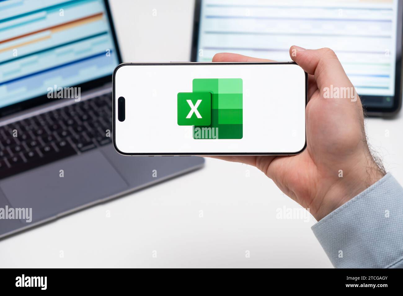 Excel logo on the screen of a smartphone in mans hand with laptop and ...