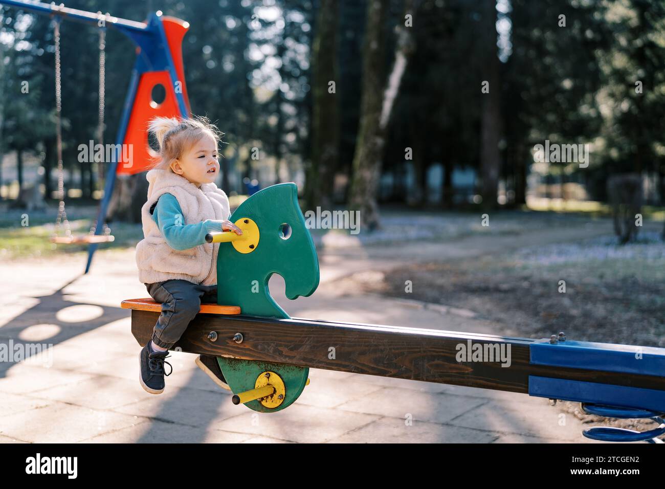 Little girl sits on a swing-balancer in the park. Side view Stock Photo ...