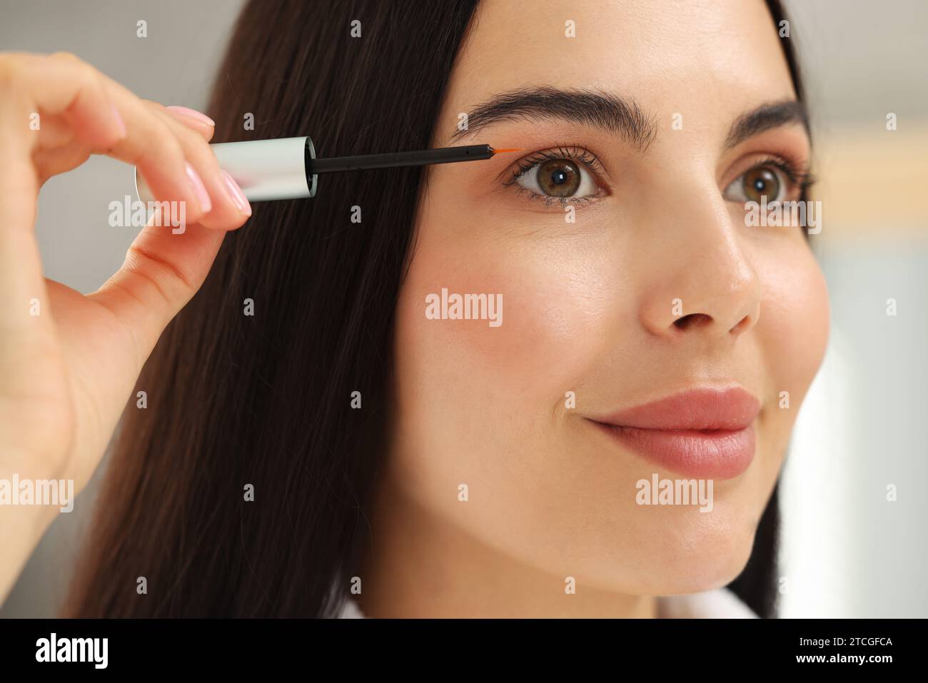 Beautiful woman applying serum onto her eyelashes indoors, closeup ...