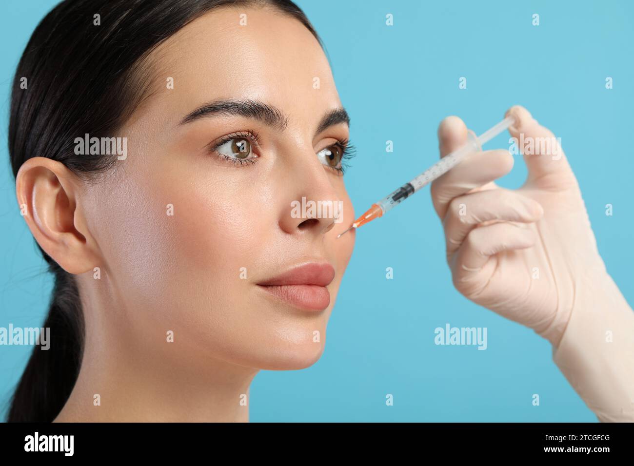 Doctor giving facial injection to young woman on light blue background ...