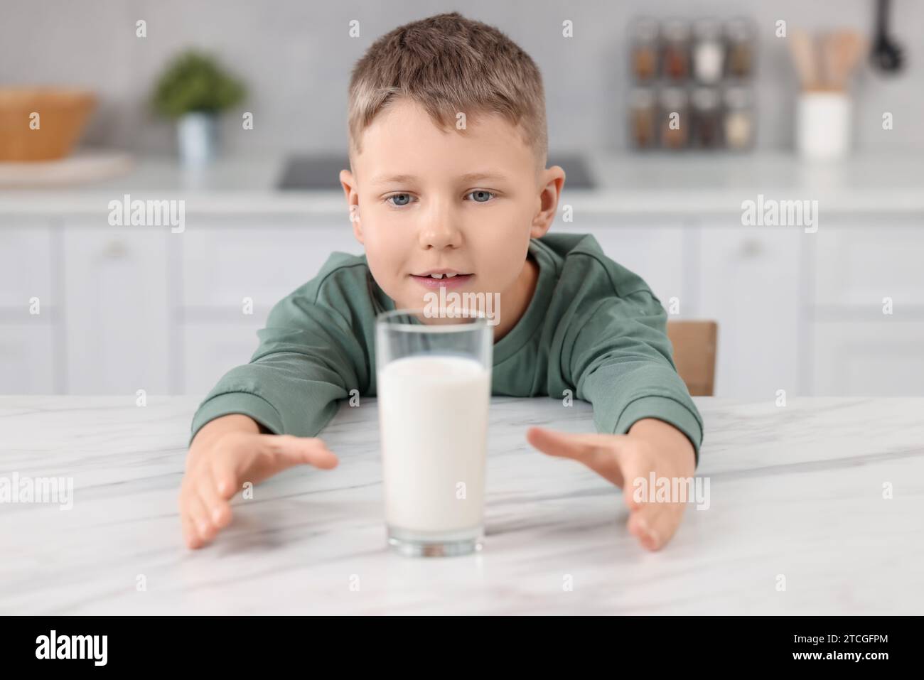 Cute boy reaching out for glass of milk at white table in kitchen Stock ...