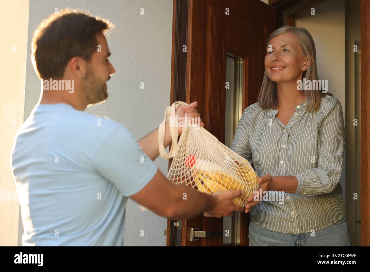 Helping neighbours. Man with net bag of products visiting senior woman ...