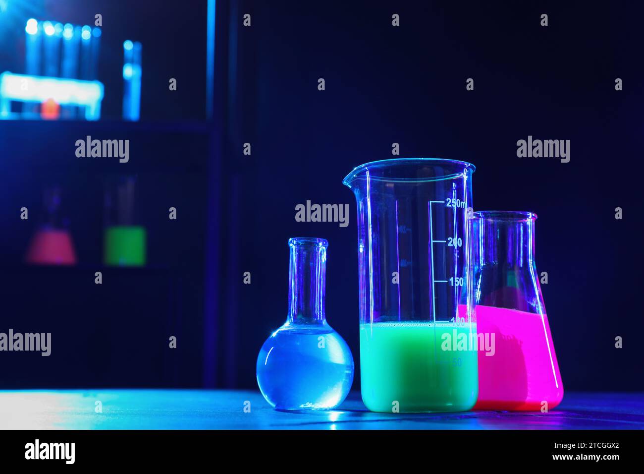 Laboratory glassware with luminous liquids on table, space for text ...