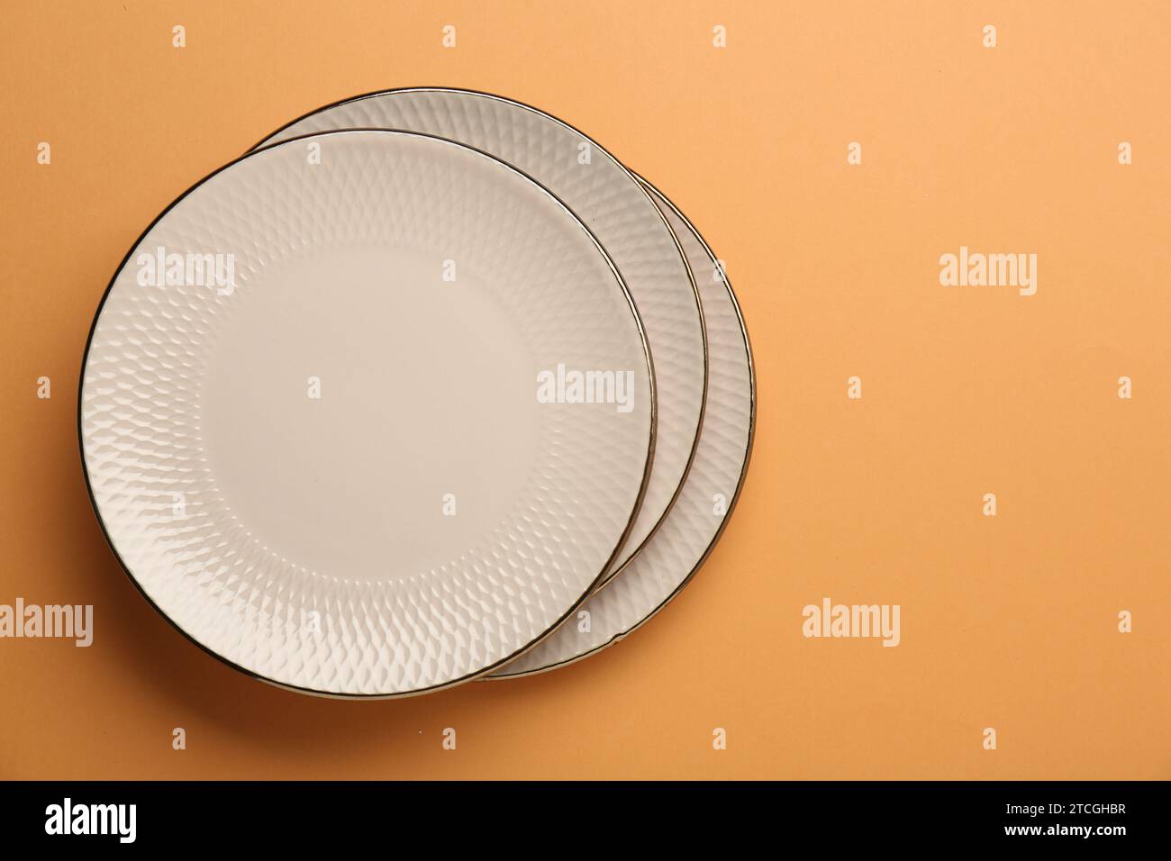 Beautiful beige ceramic plates on orange background, top view. Space ...