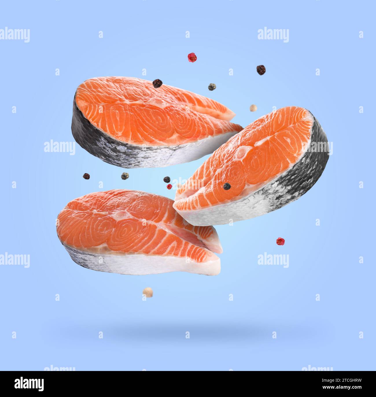 Fresh salmon steaks and peppercorns falling on light blue background ...