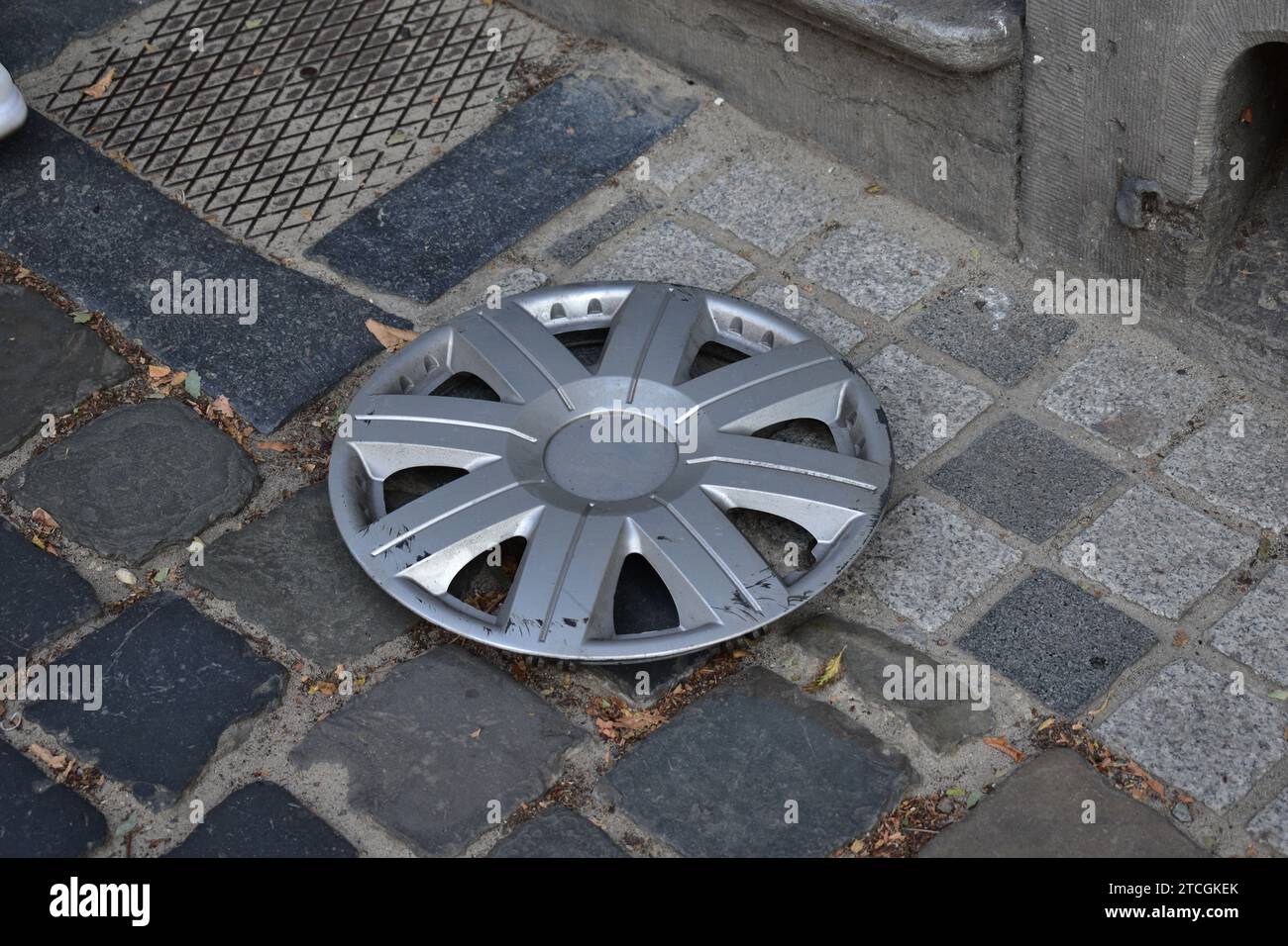 Scratched up grey plastic wheel cover laying on a cobblestone sidewalk ...