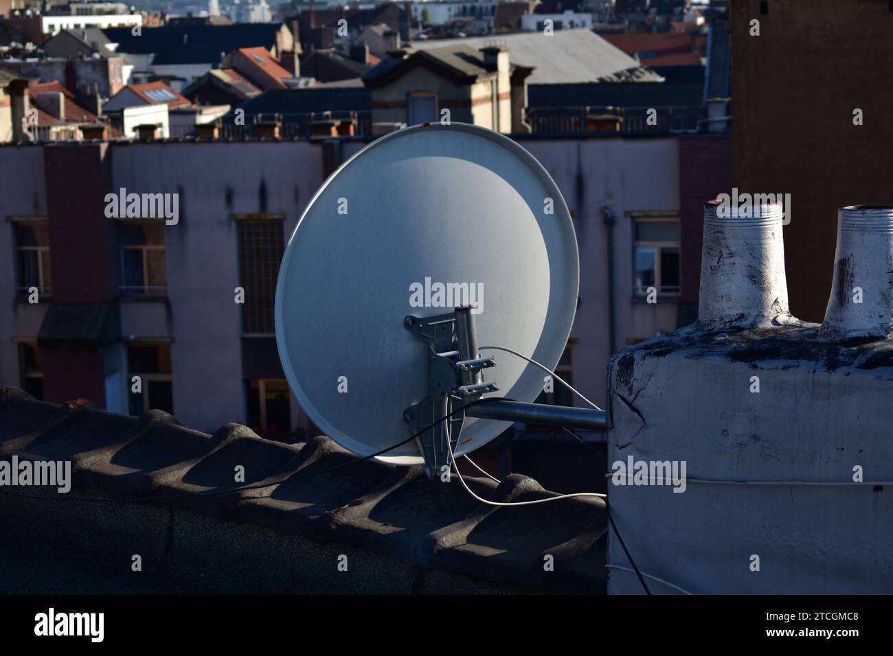 Rear view of a grey satellite dish on a building roof with urban ...