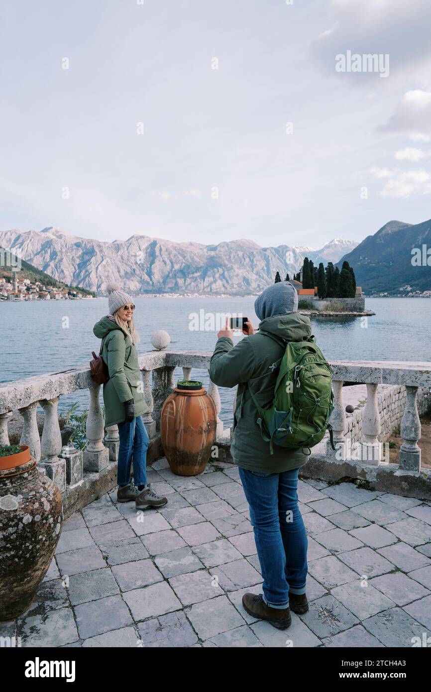 Man takes a picture of woman leaning on a balustrade by the sea. Back ...
