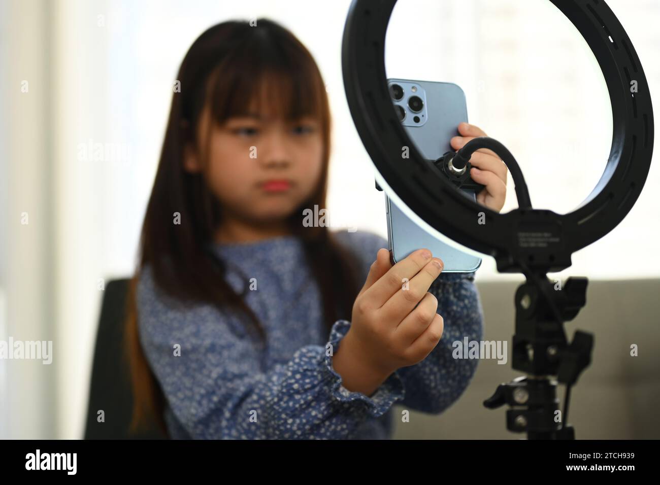 Smiling asian girl talking to camera of mobile phone on tripod ...