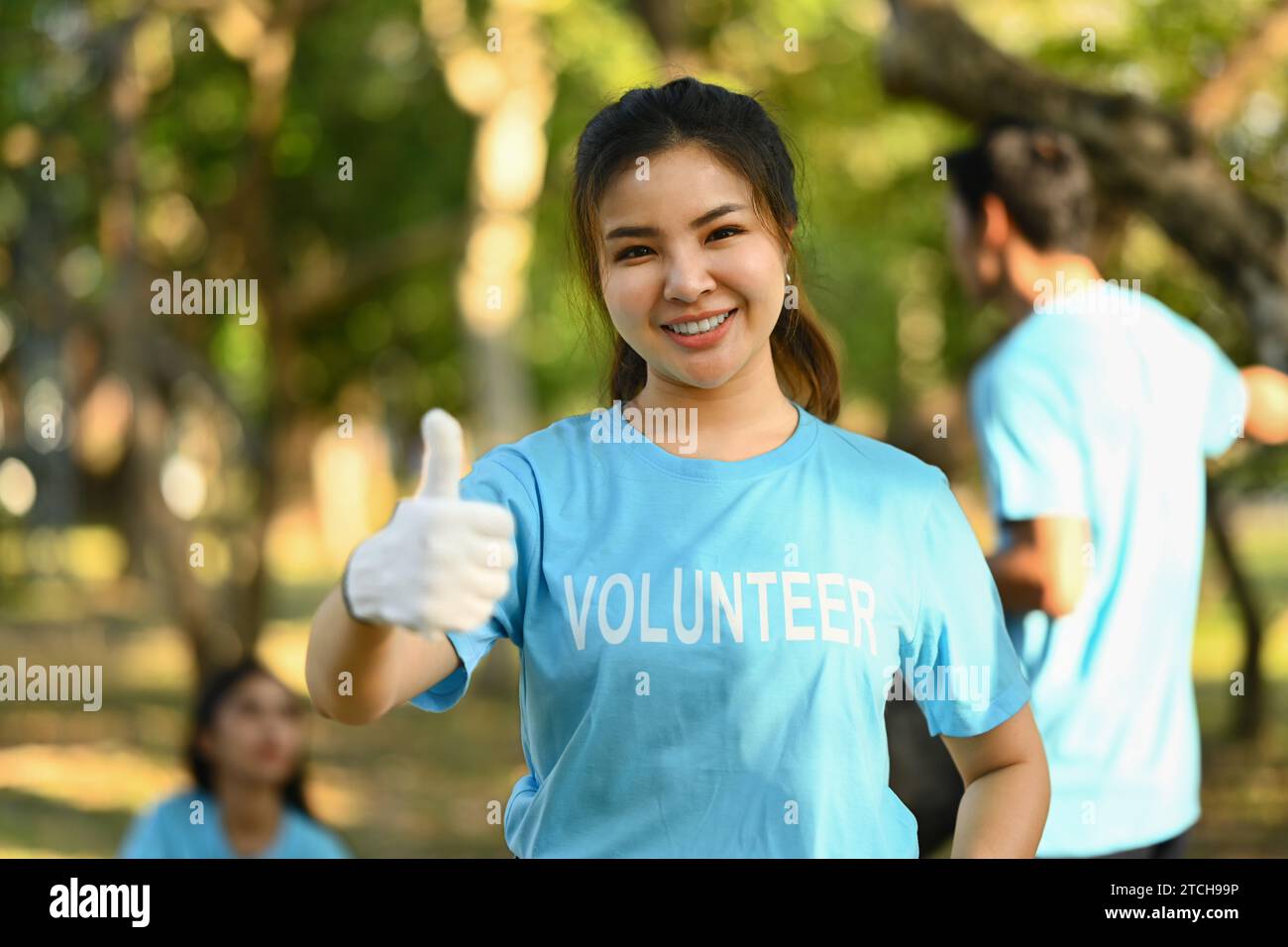 Beautiful Asian female activist in volunteer t-shirt showing thumbs up standing outdoor Stock ...