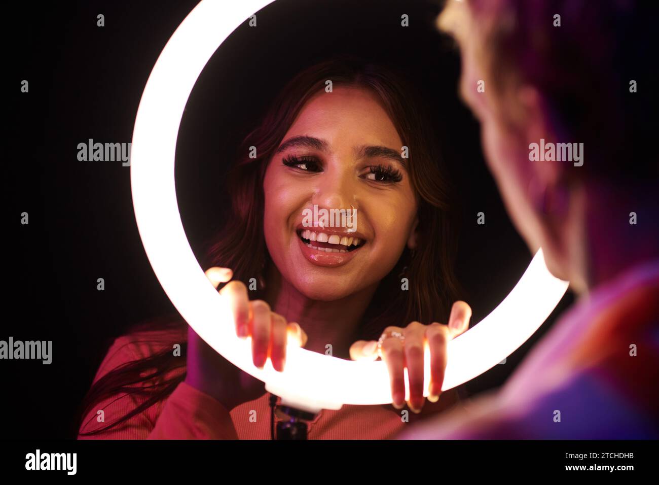 Smiling young woman looking at boyfriend through ring light Stock Photo ...