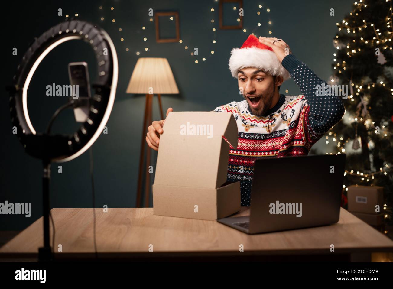 Happy muslim male blogger wearing Santa Claus hat unpacking gift boxes ...