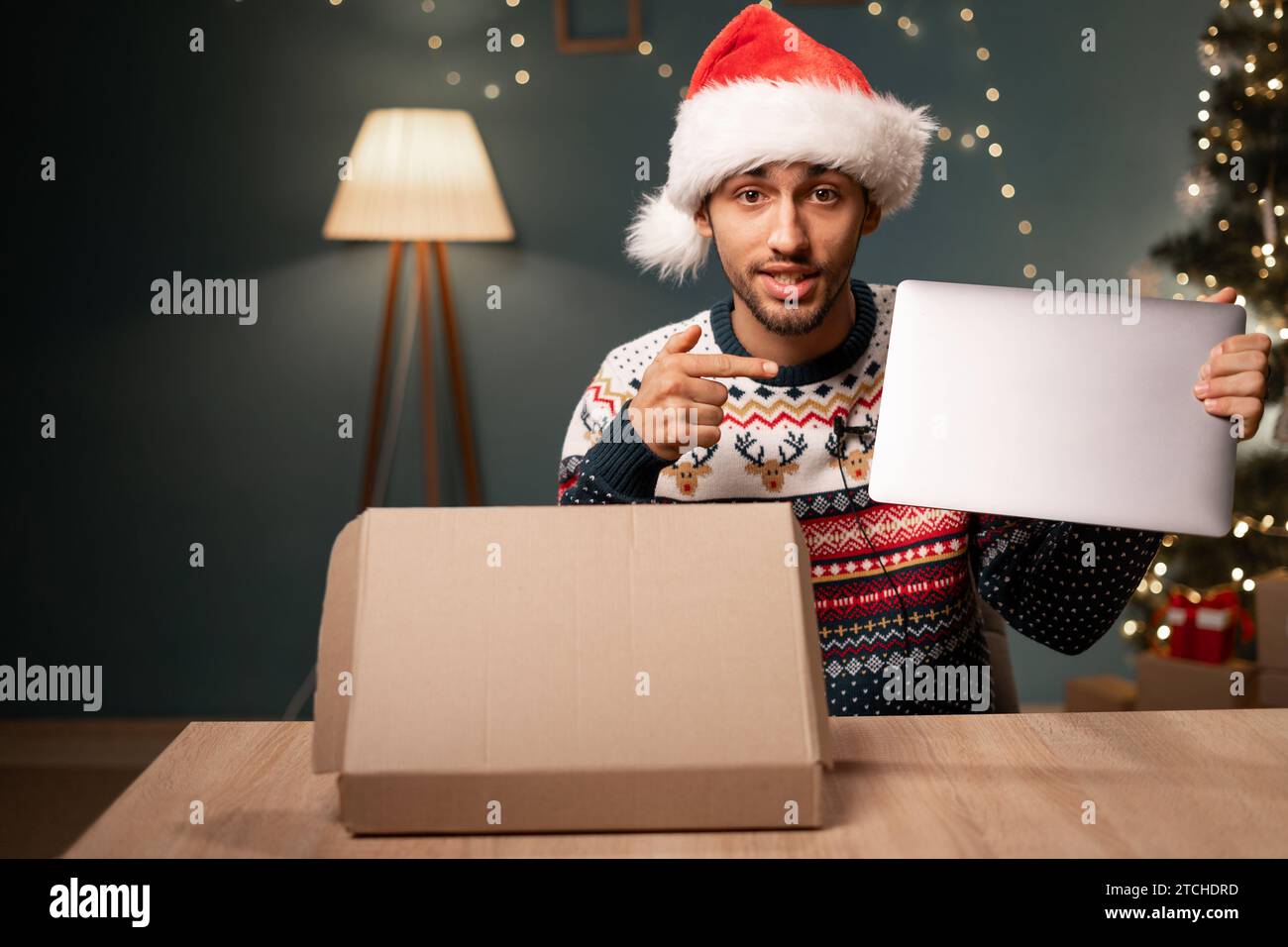 Male vlogger in Santa hat looking at camera filming clip of unboxing ...