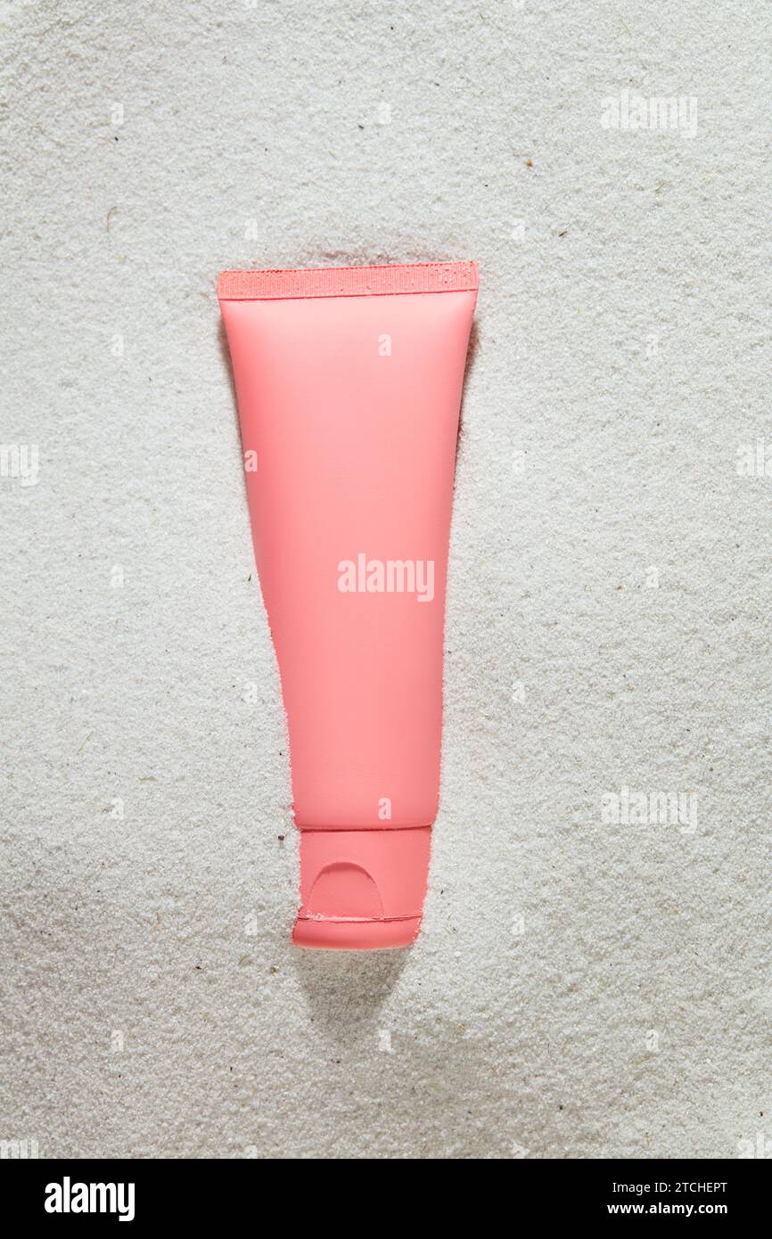 View from above of pink tube of sunscreen without label on beach sand ...