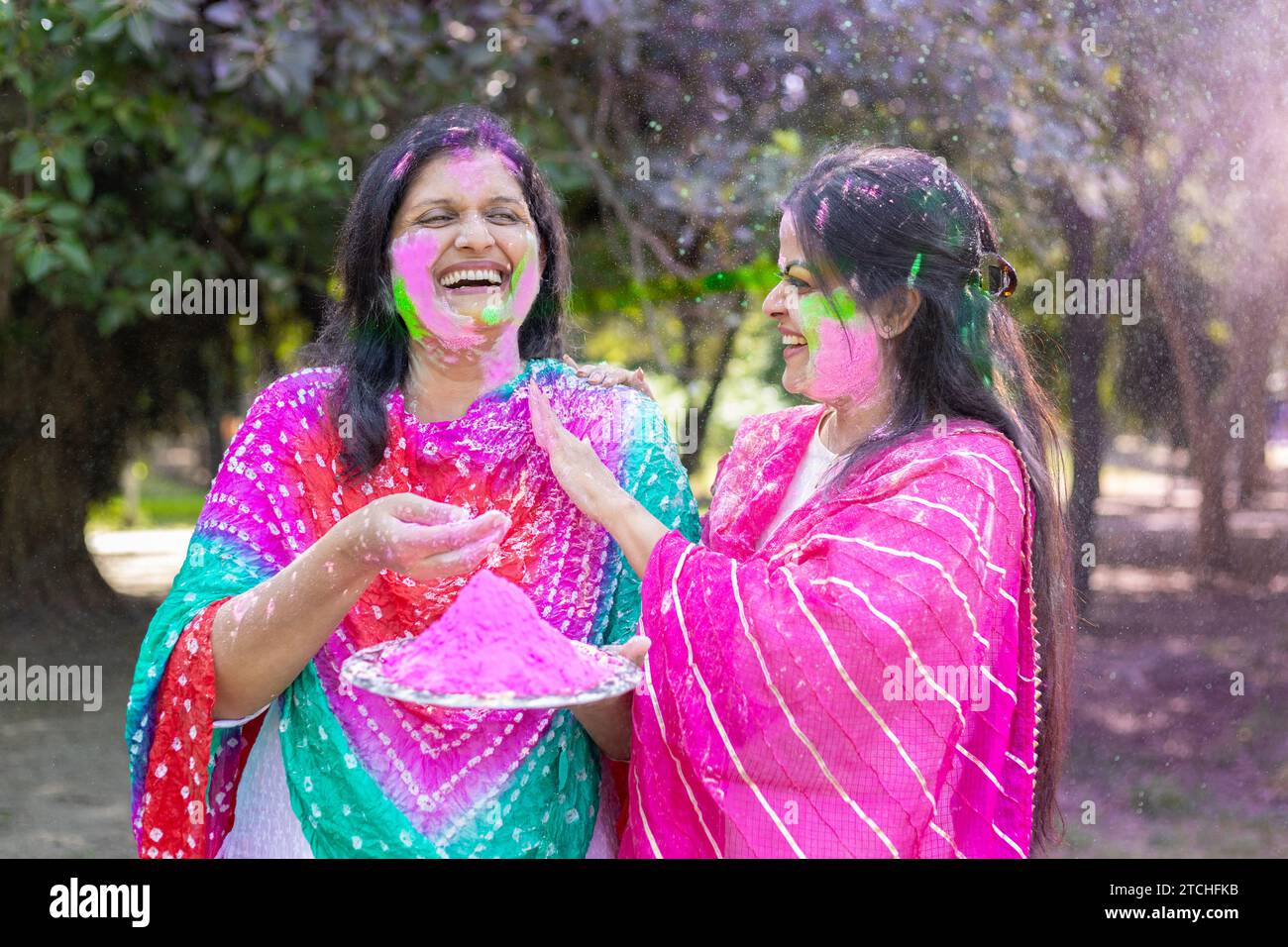 Two Happy indian women wearing white kurta holding plate of color ...