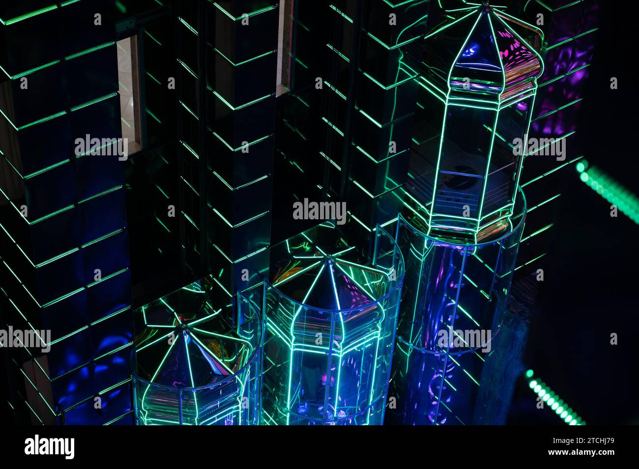 Green and blue neon cyberpunk light in interior of a modern building with an glass elevator ...