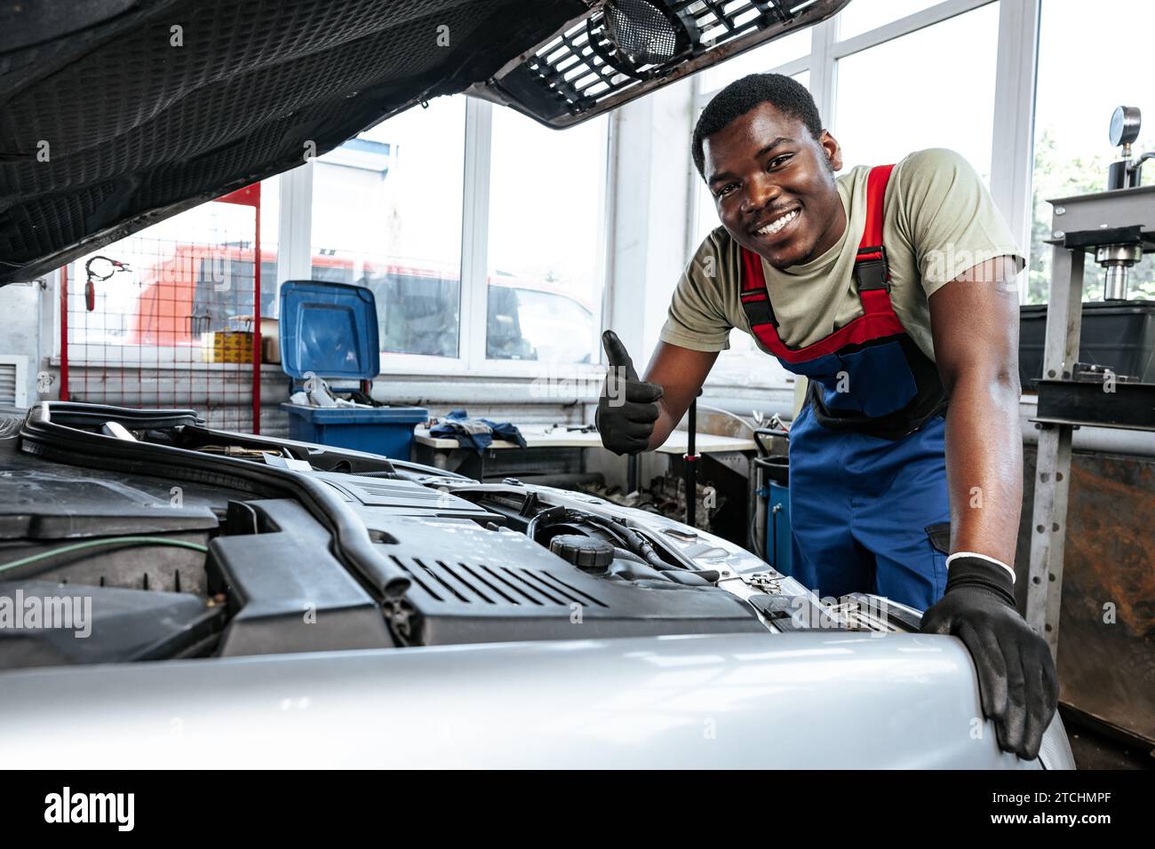 Young African man working under the hood of car fixing engine in auto ...
