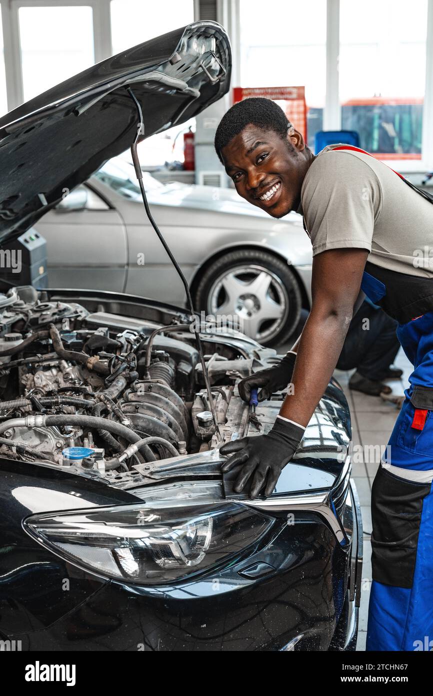 Young African man working under the hood of car fixing engine in auto ...