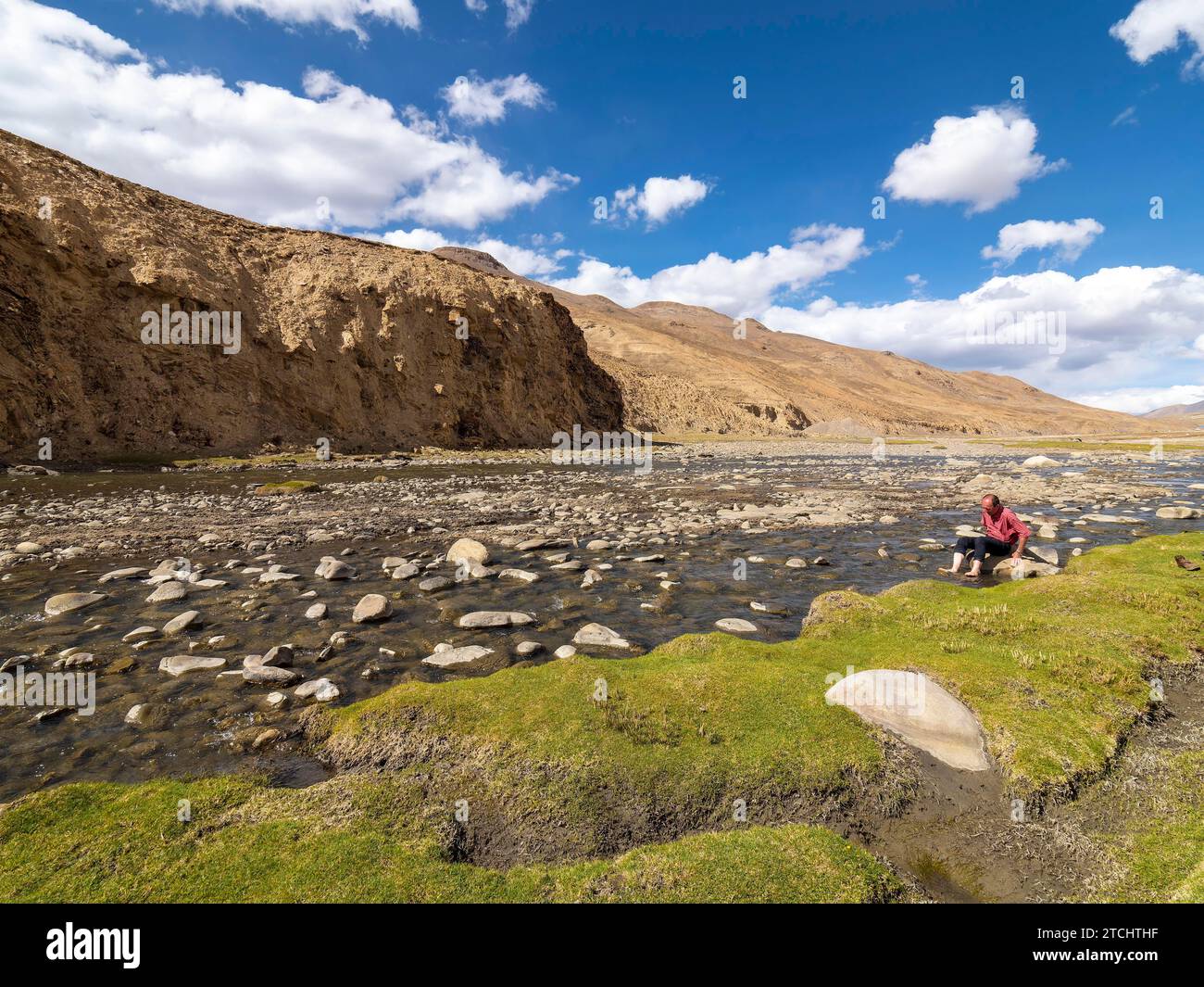 Man bathing his feet in the river, high mountains at Ximila Pass, Tibet ...
