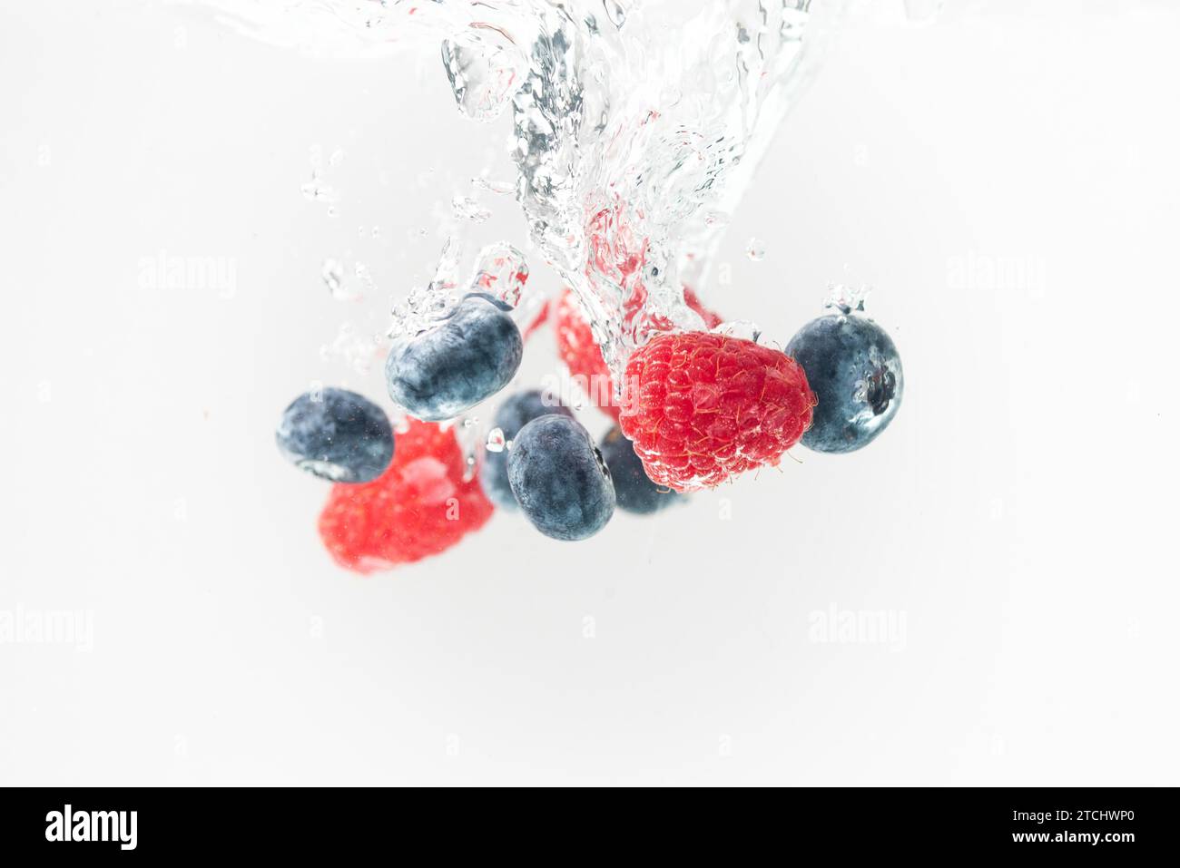 Blueberry?s and raspberries splashing into crystal clear water with air ...