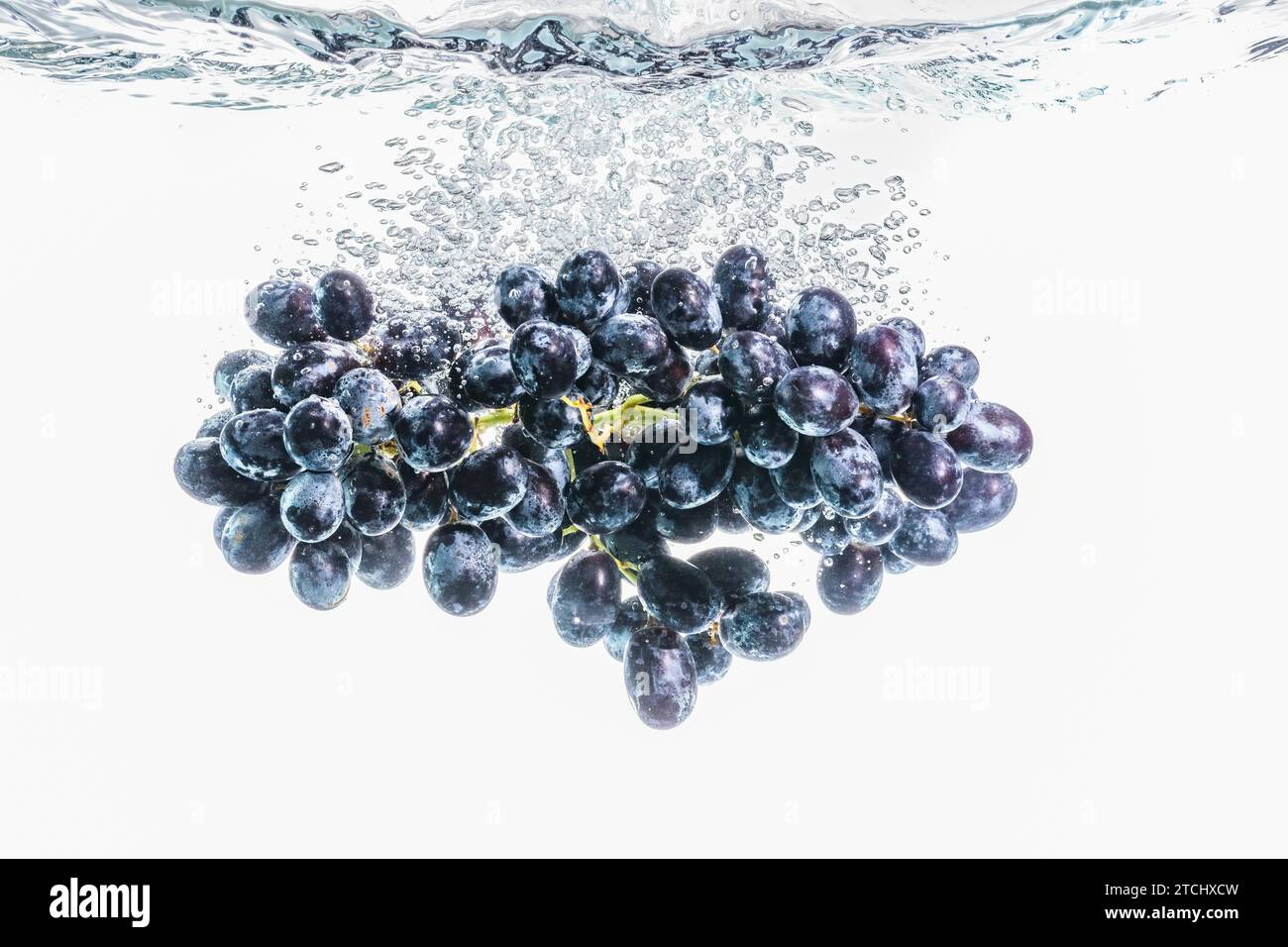 Bunch of red grapes splashing into crystal clear water on withe ...