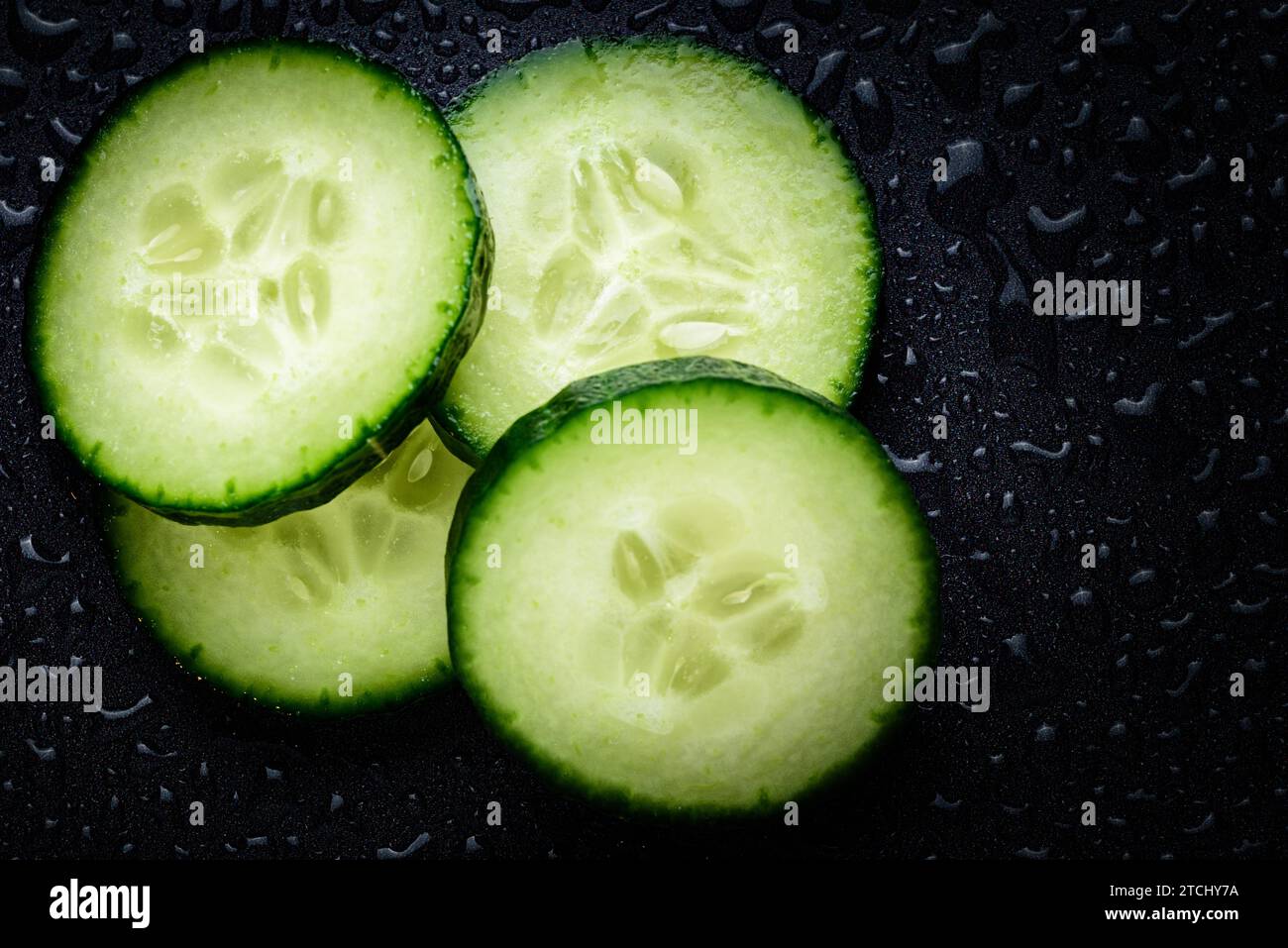 Cucumber slices. Pieces of fresh cucumber on black wet table with water ...
