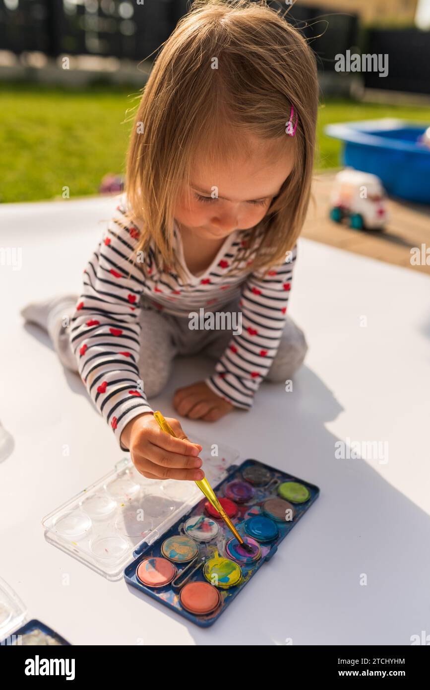 Focused Child with mother painting with poster paint outdoors on the ground on big sheet of ...