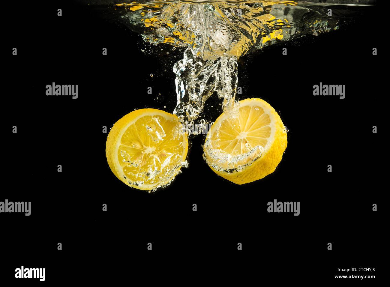 Fresh yellow lemon halves in water splashing isolated on black ...