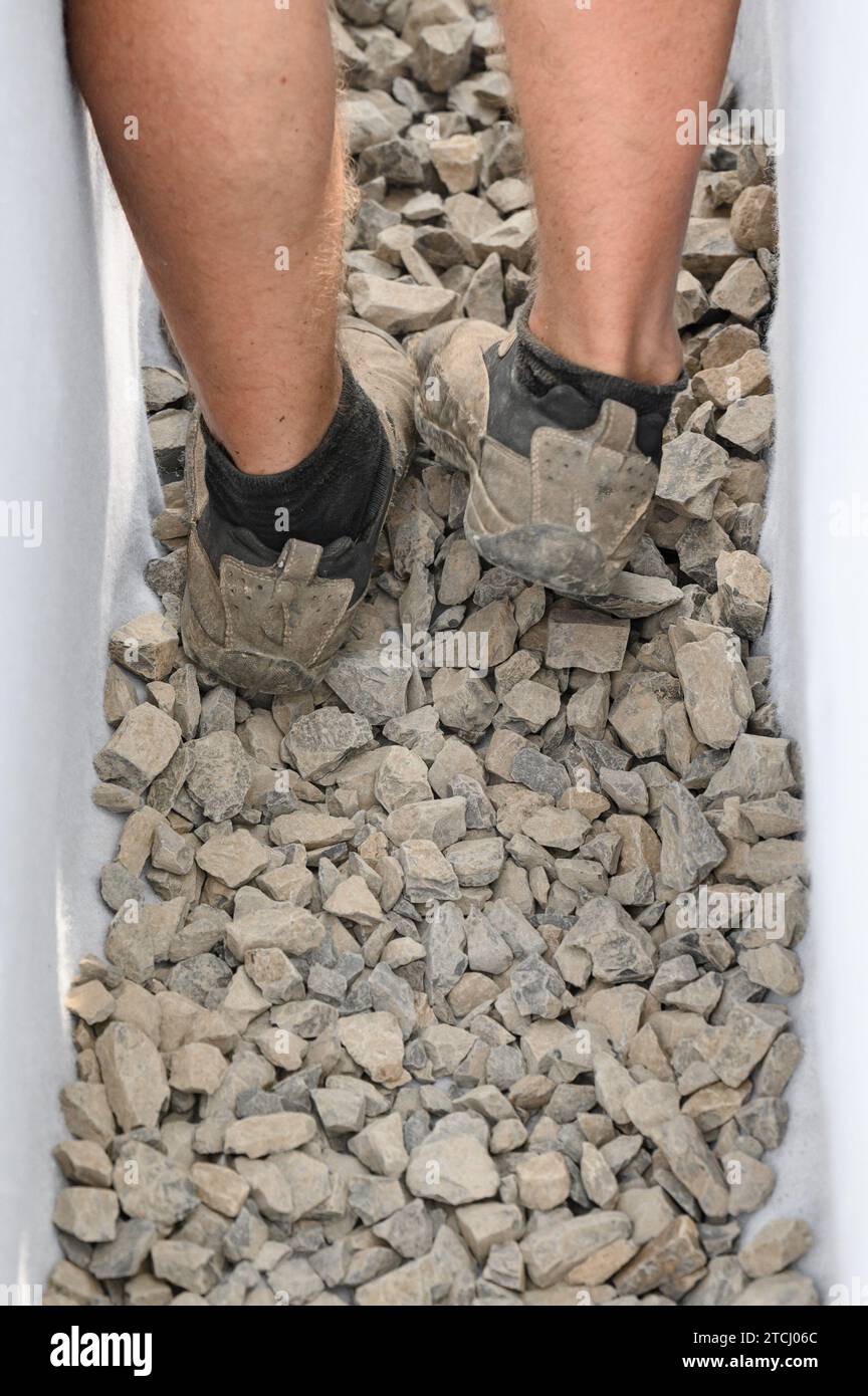 A worker stands in a drainage trench with white geotextile. Feet of the ...