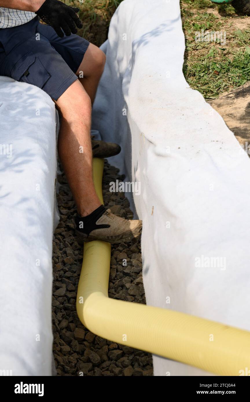 A worker stands in a drainage trench with white geotextile. Feet of the ...