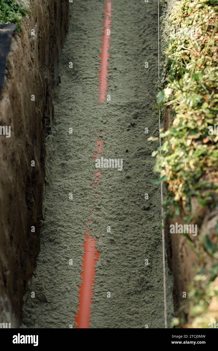 An orange reinforced sewer pipe is compacted with sand in a trench ...