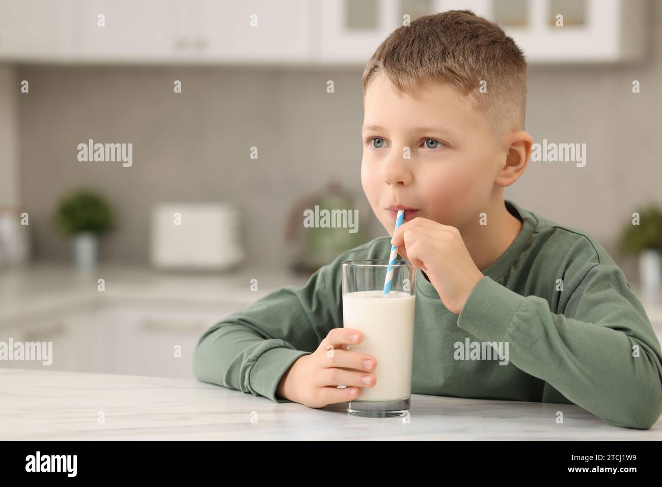Cute boy drinking fresh milk from glass at white table in kitchen ...