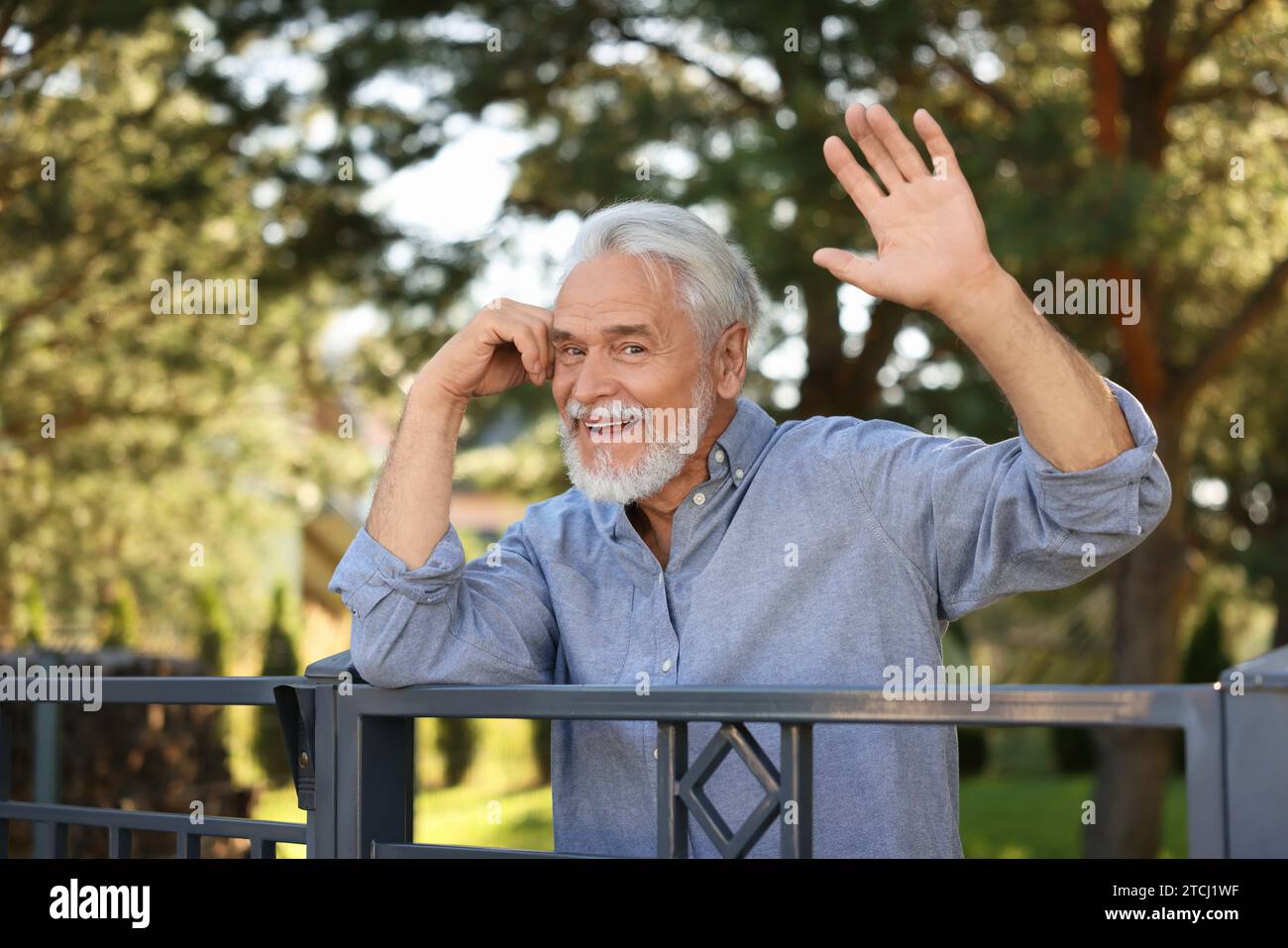 Neighbor greeting. Happy senior man waving near fence outdoors Stock ...