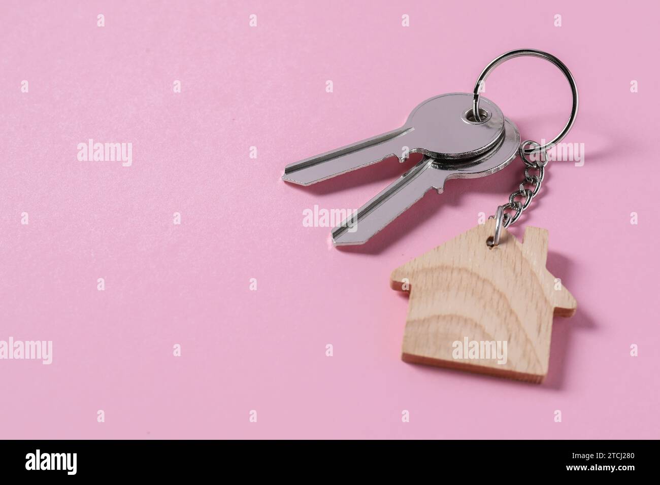 Metallic keys with wooden keychain in shape of house on pink background ...