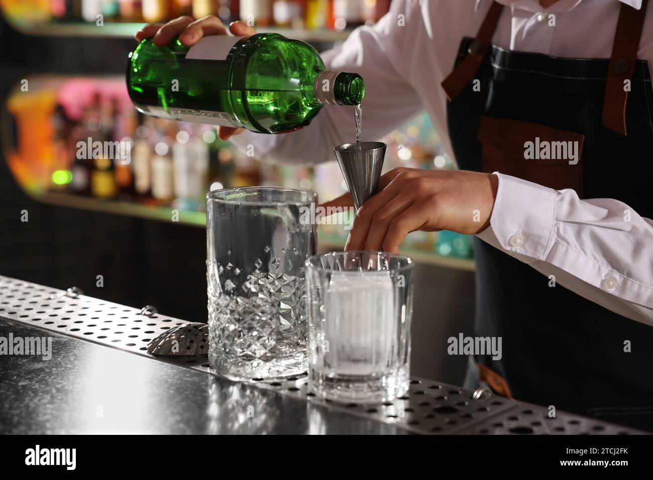 Cocktail making. Bartender pouring alcohol from bottle into jigger at counter in bar, closeup ...