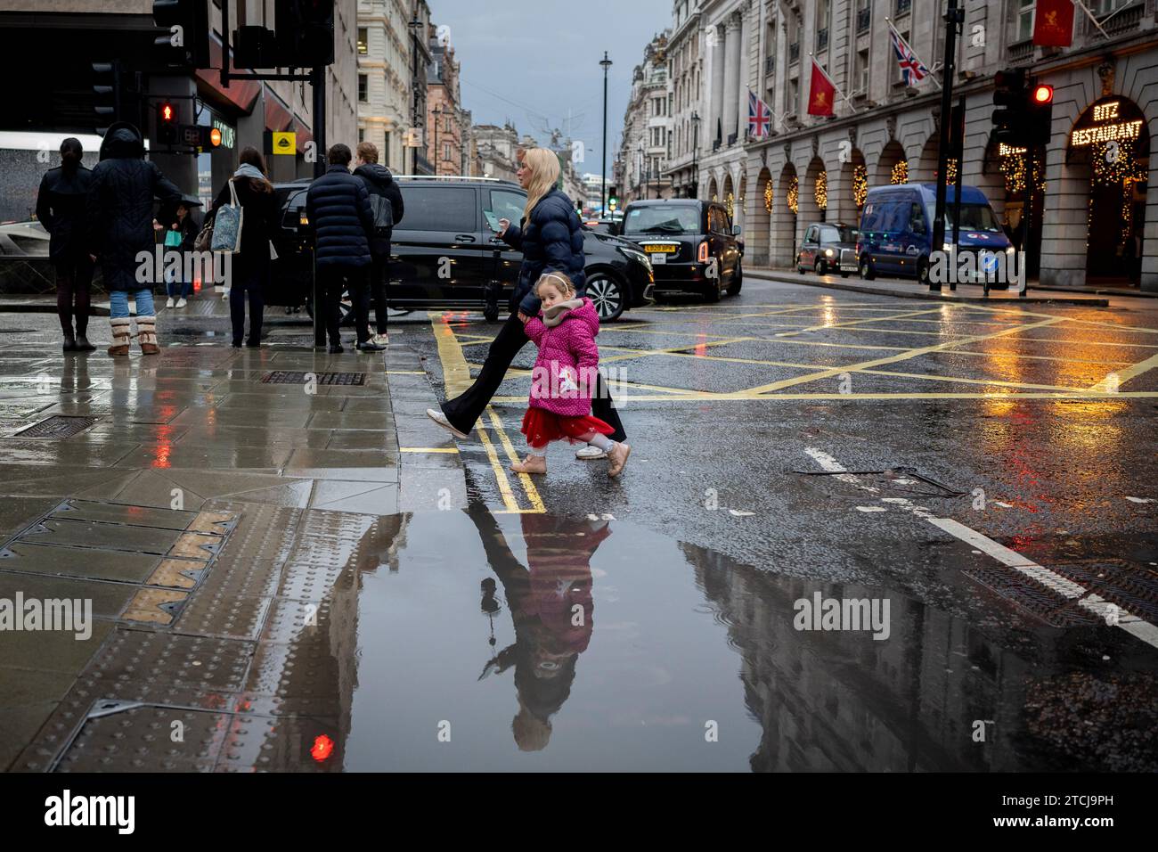 A woman walks with a child to cross the road alongside a puddle on ...
